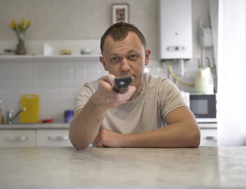 Young Guy with a TV Remote Control Switches Channels while Sitting in ...