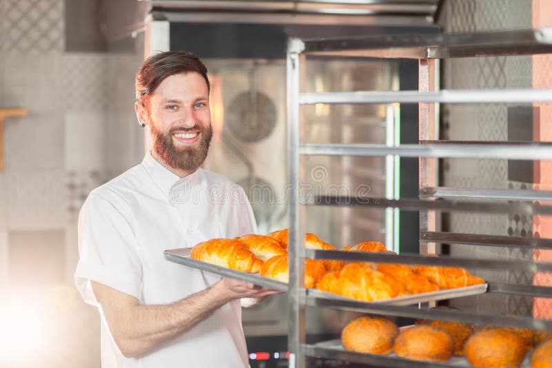 A Young Handsome Baker Takes Out Hot Fresh Baking from the Oven in the ...