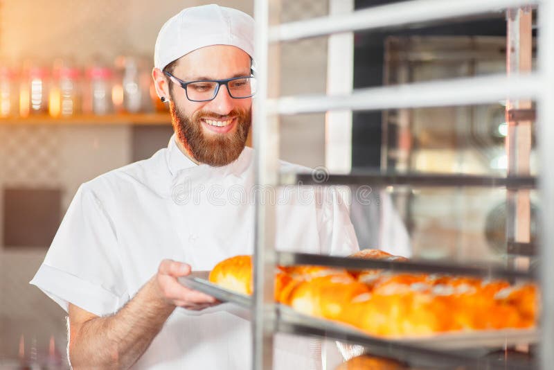 A Young Handsome Baker Takes Out Hot Fresh Baking from the Oven in the ...