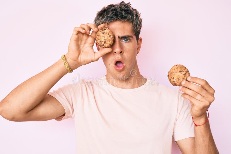 Young Handsome Man Holding Cookie in Shock Face, Looking Skeptical and ...