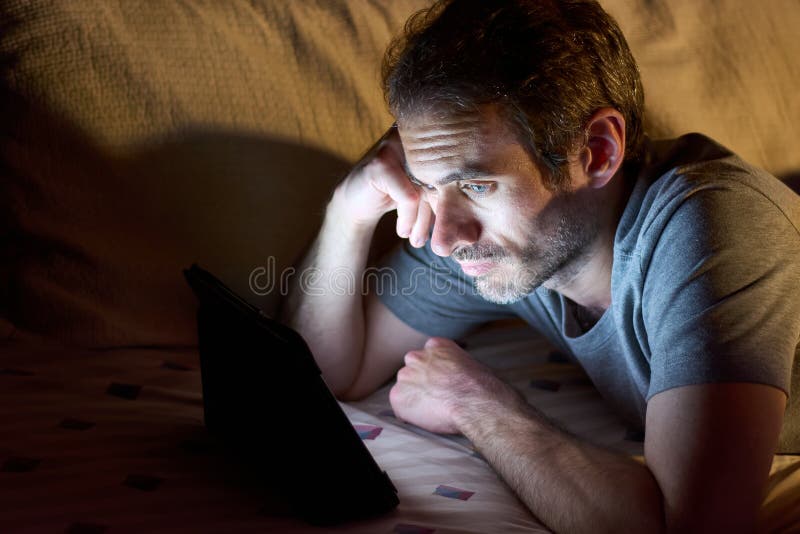 Young Handsome Man Lying in Bed at Night while Watching Something on a ...
