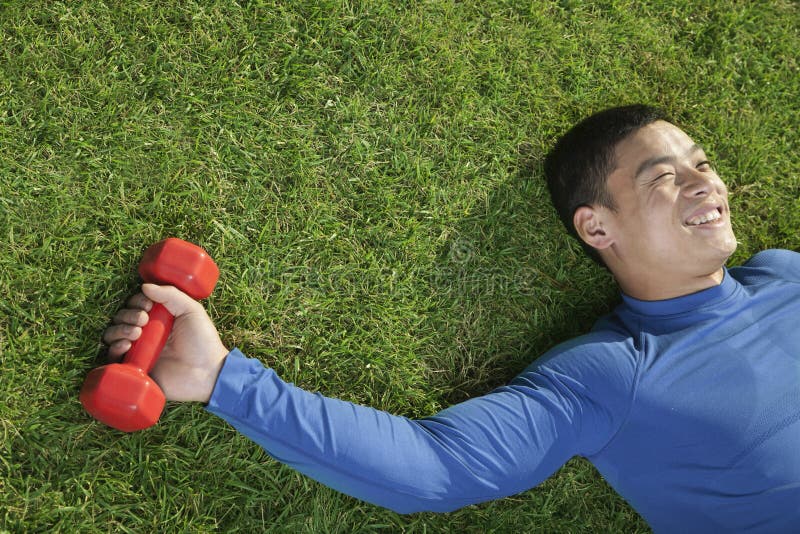 Young Happy Athletic Man Lying Down in Grass with Red Dumbbell, View ...