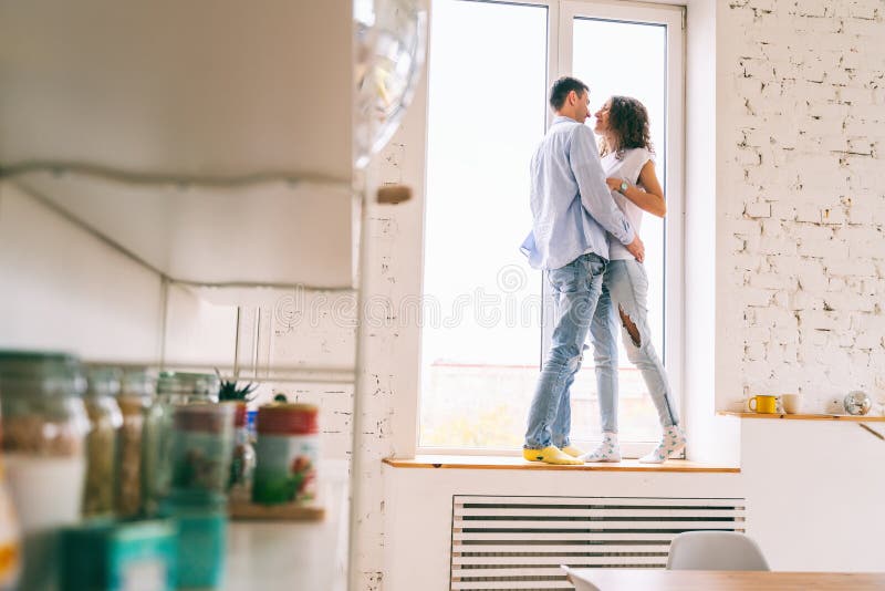 Young Happy Couple Hugging On The Windowsill In Their Apartment