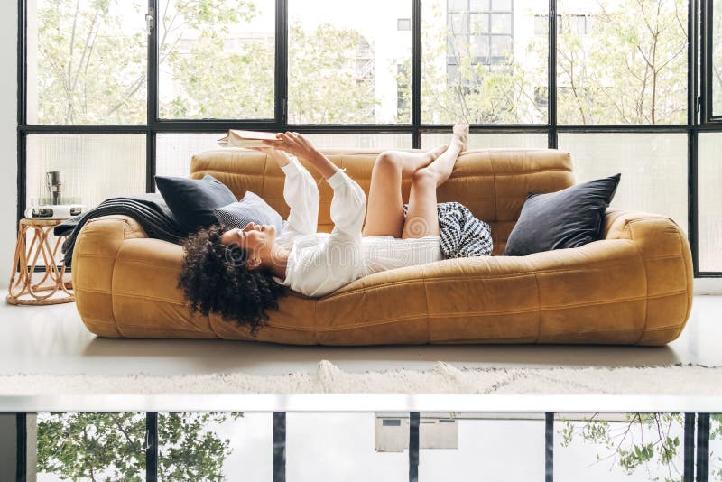 Young Happy Multiracial Woman Lying on Sofa with Legs Up, Reading a ... Young Happy Multiracial Woman Lying on Sofa with Legs Up, Reading a ...