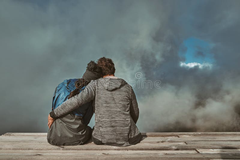 A Young Hikers Sitting High in the Mountains Hugging and Looking at the ...