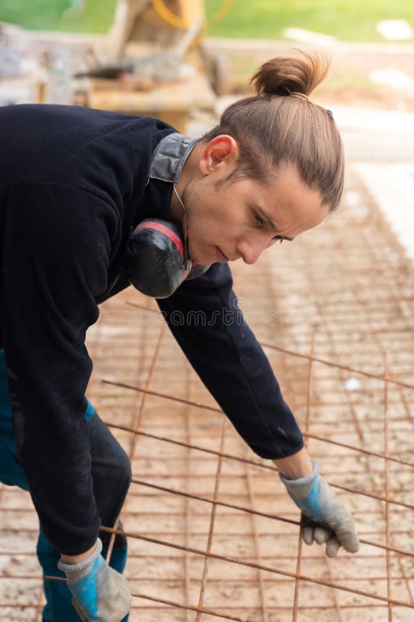 Young Hipster Apprentice Working in Construction Placing Iron Mesh Grid ...