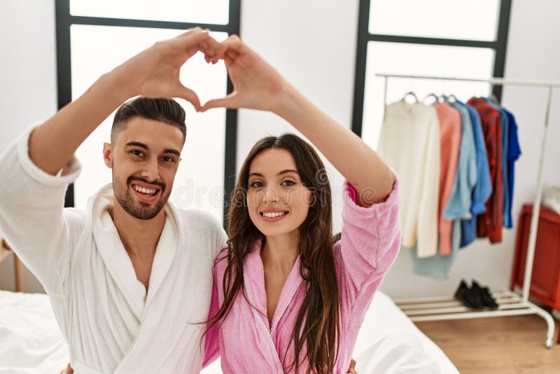 Young Hispanic Couple Doing Heart Symbol with Hands Sitting on the Bed ...