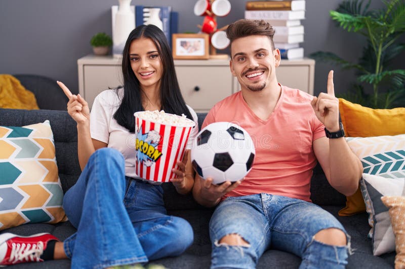 Young Hispanic Couple Football Hooligans Holding Ball And Eating