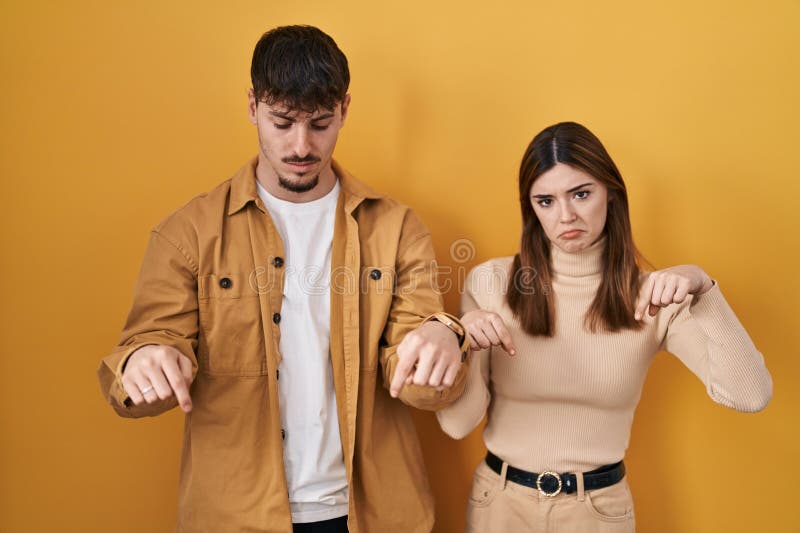 Young Hispanic Couple Standing Over Yellow Background Pointing Down ... Young Hispanic Couple Standing Over Yellow Background Pointing Down ...