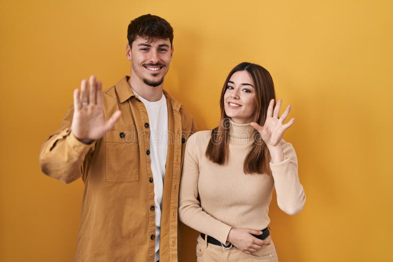 Young Hispanic Couple Standing Over Yellow Background Waiving Saying ... Young Hispanic Couple Standing Over Yellow Background Waiving Saying ...