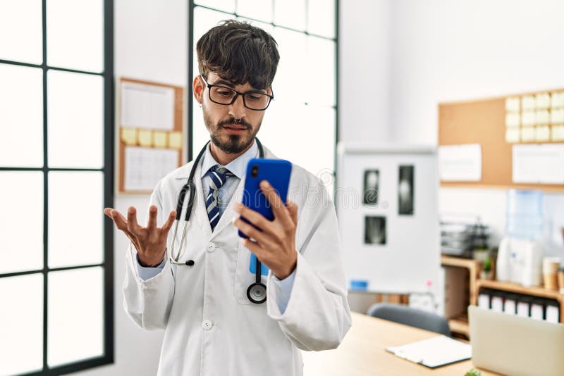 Young Hispanic Doctor Man Having Video Call Using Smartphone at Clinic ...
