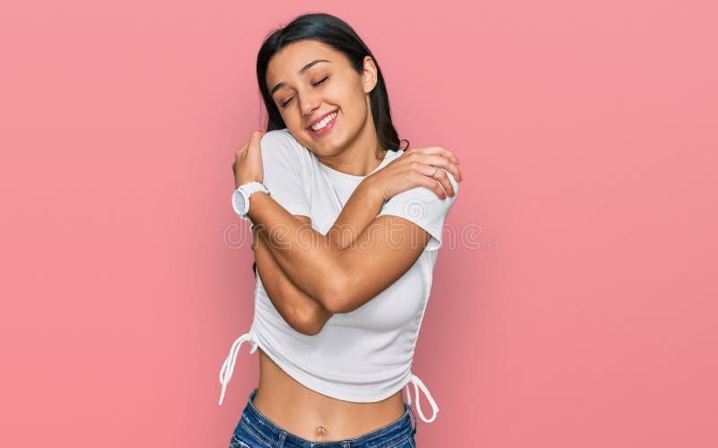 Young Hispanic Girl Wearing Casual White T Shirt Hugging Oneself Happy