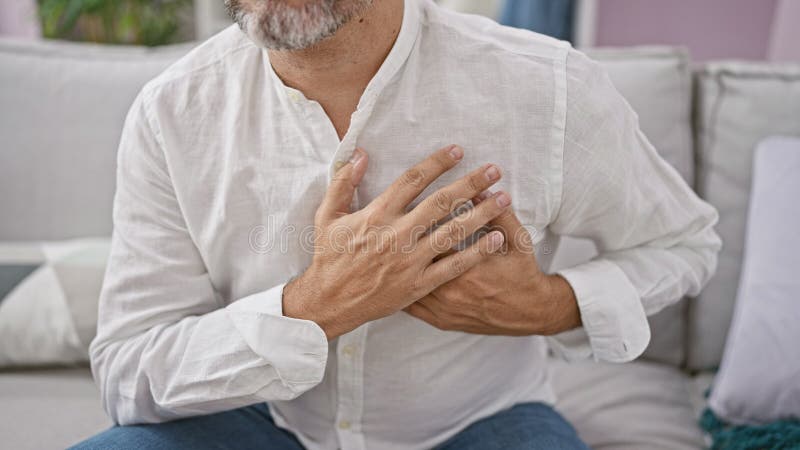 Young Hispanic Grey-haired Man Sitting on Sofa Suffering Heart Attack ...