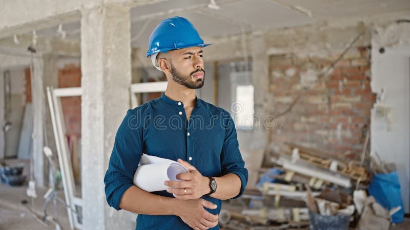 Young Hispanic Man Architect Wearing Hardhat Holding Blueprints at ...
