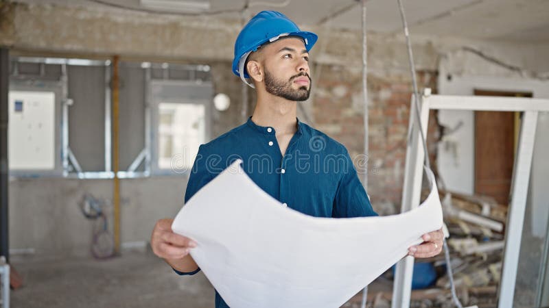 Young Hispanic Man Architect Wearing Hardhat Looking at Blueprints at ...