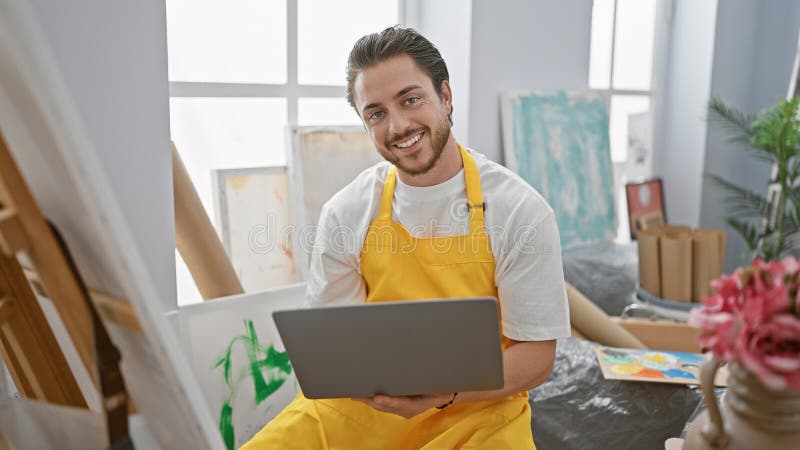 Young Hispanic Man Artist Using Laptop Smiling at Art Studio Stock ...