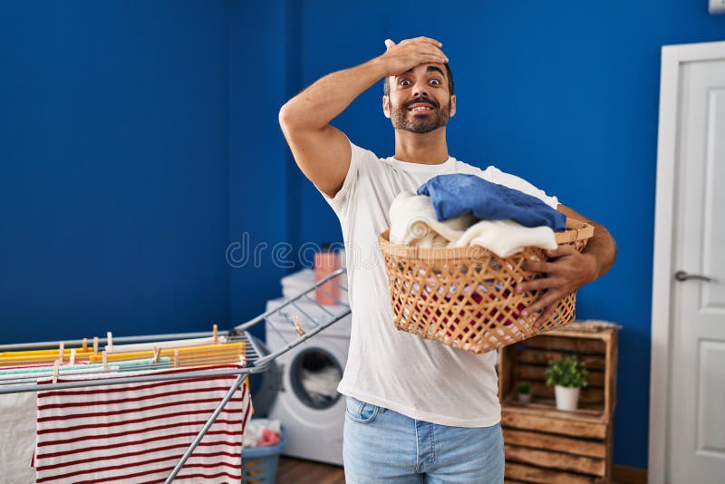 Young Hispanic Man With Beard Holding Laundry Basket Stressed And Frustrated With Hand On Head