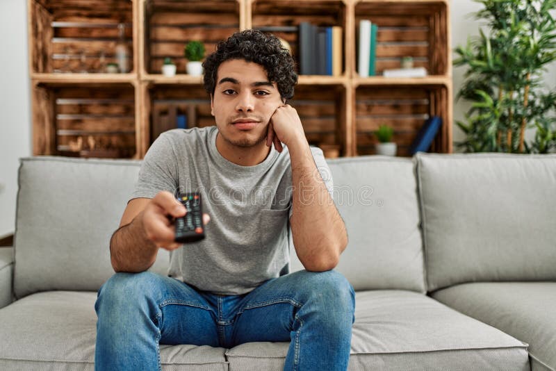 Young Hispanic Man Bored Watching Tv Sitting on the Sofa at Home Stock ...