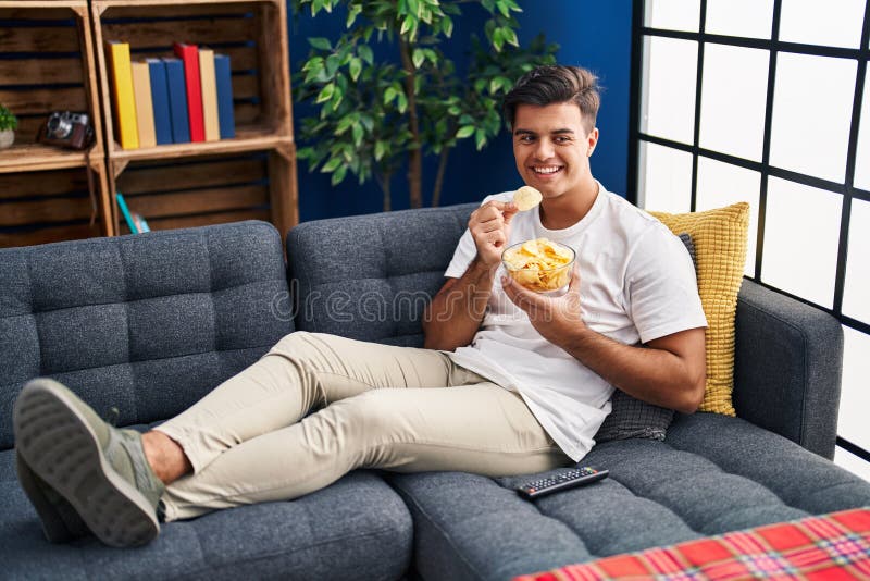 Young Hispanic Man Eating Chips Potatoes Sitting on Sofa at Home Stock ...