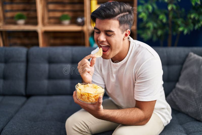 Young Hispanic Man Eating Chips Potatoes Sitting on Sofa at Home Stock ...