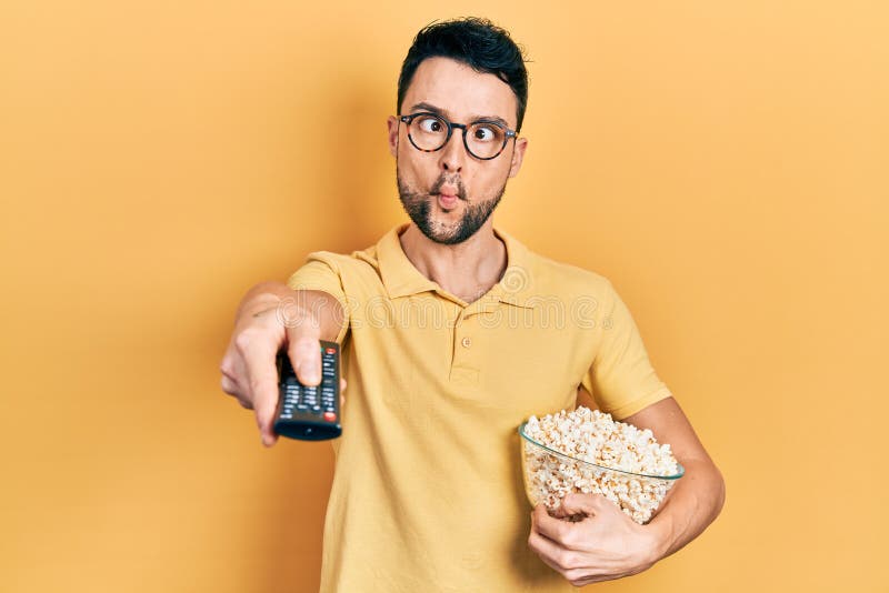 Young Hispanic Man Eating Popcorn Using Tv Control Making Fish Face ...