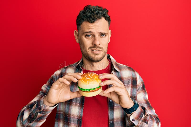 Young Hispanic Man Eating a Tasty Classic Burger Clueless and Confused ...