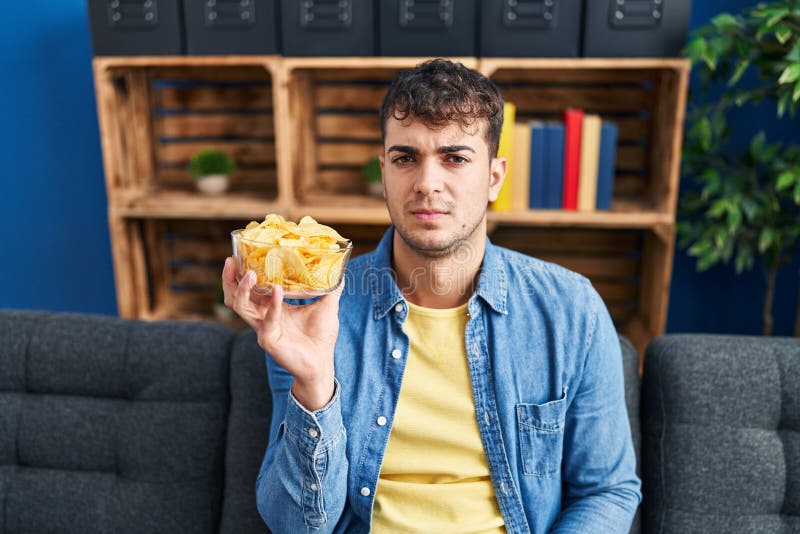 Young Hispanic Man Holding Potato Chips Thinking Attitude and Sober ...