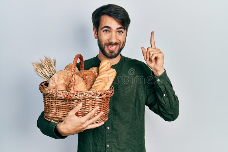 Young Hispanic Man Holding Wicker Basket with Bread Smiling with an ...