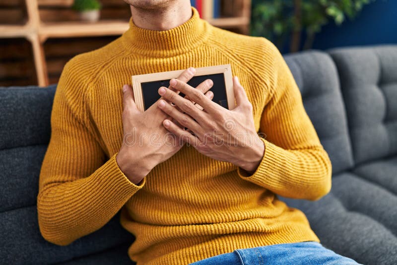 Young Hispanic Man Hugging Photo Frame Sitting on Sofa at Home Stock ...