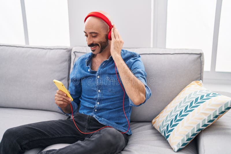 Young Hispanic Man Listening To Music Sitting On Sofa At Home Stock