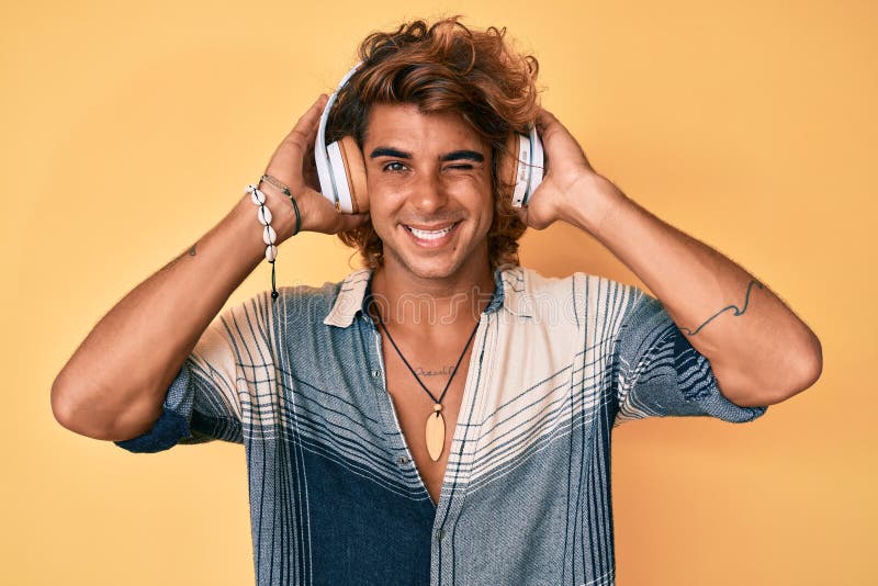 Young Hispanic Man Listening To Music Using Headphones Winking Looking