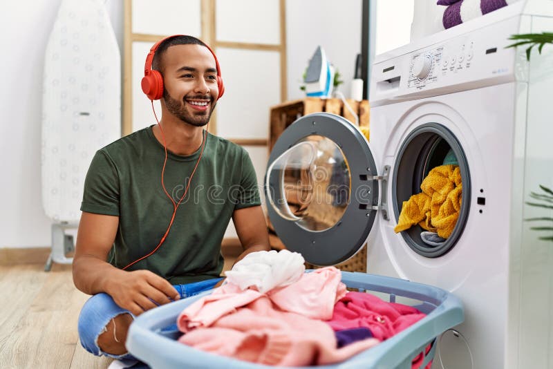 Young Hispanic Man Listening To Music Using Washing Machine at Laundry ...