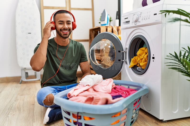 Young Hispanic Man Listening To Music Using Washing Machine at Laundry ...