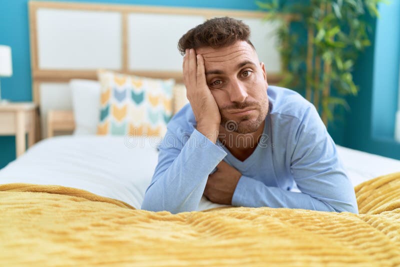 Young Hispanic Man Lying on Bed with Tired Expression at Bedroom Stock ...