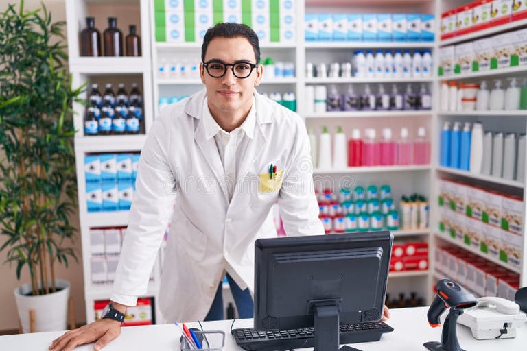 Young Hispanic Man Pharmacist Smiling Confident Using Computer at ...