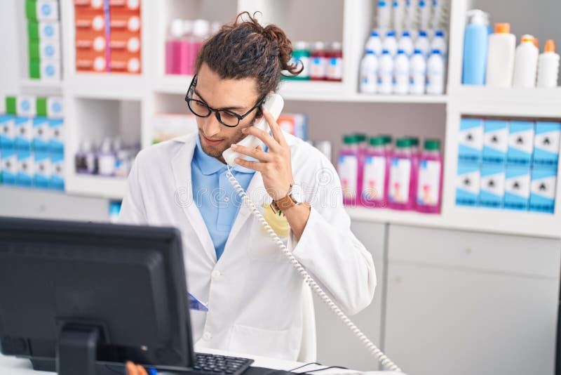 Young Hispanic Man Pharmacist Talking on Telephone Using Computer at ...