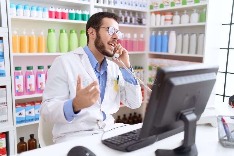 Young Hispanic Man Pharmacist Talking on Telephone Using Computer at ...