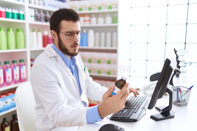 Young Hispanic Man Pharmacist Using Computer Holding Medication Bottle ...