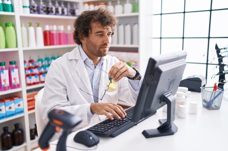 Young Hispanic Man Pharmacist Using Computer at Pharmacy Stock Image ...