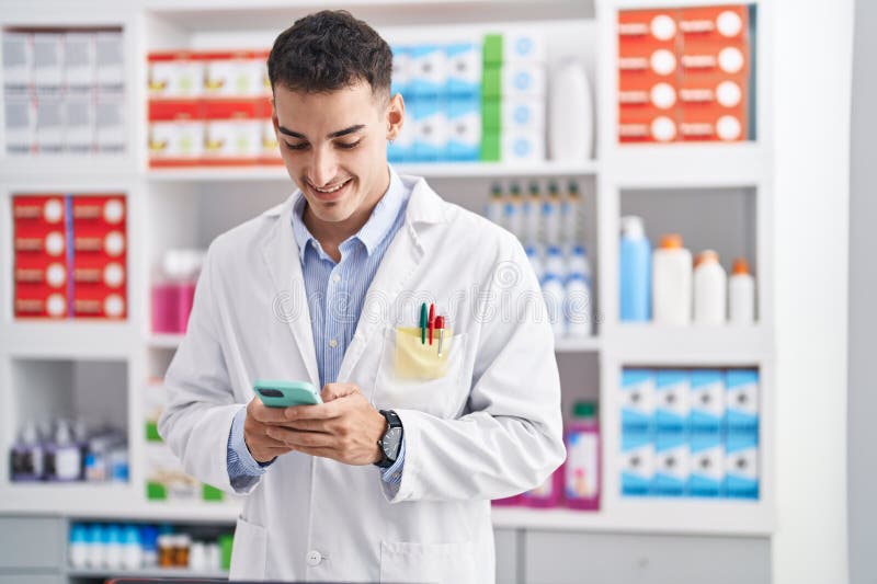Young Hispanic Man Pharmacist Using Smartphone Working at Pharmacy ...