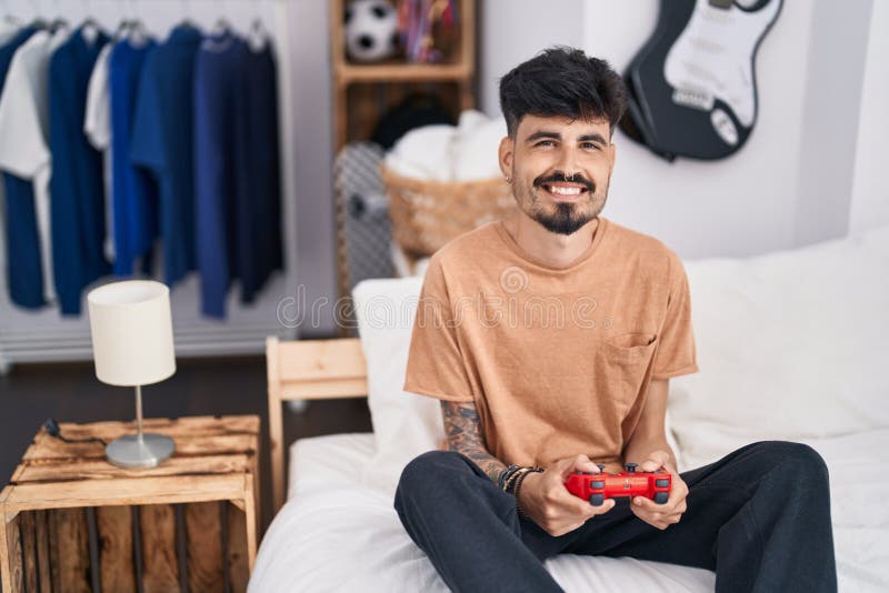 Young Hispanic Man Playing Video Game Sitting on Bed at Bedroom Stock ...