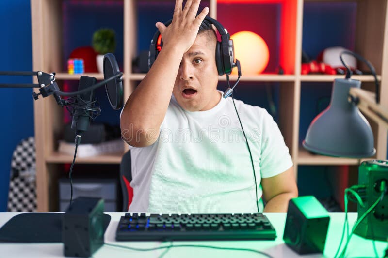 Young Hispanic Man Playing Video Games Surprised with Hand on Head for ...