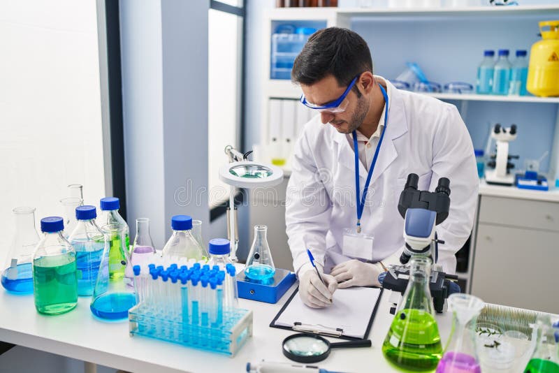 Young Hispanic Man Scientist Measuring Liquid Writing Report at ...