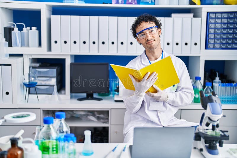 Young Hispanic Man Scientist Reading Book at Laboratory Stock Photo ...
