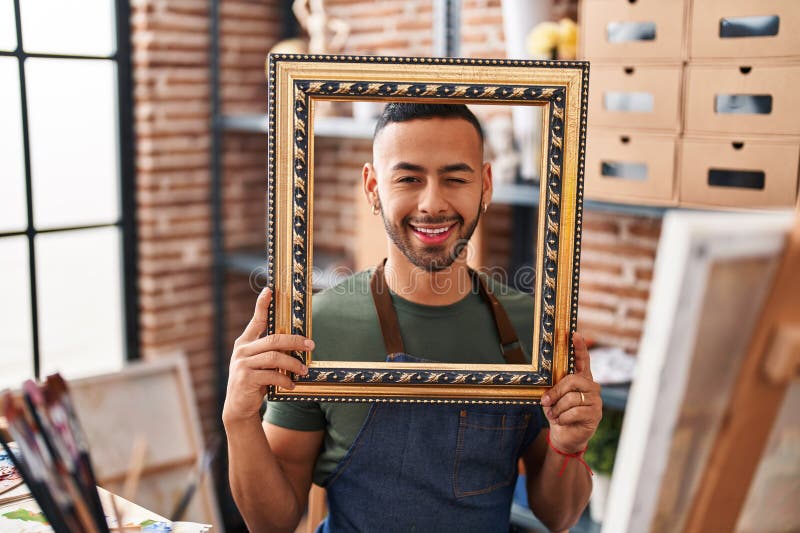 Young Hispanic Man Sitting at Art Studio with Empty Frame Winking ...