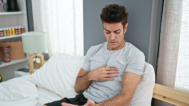 Young Hispanic Man Sitting on Bed Suffering Heart Attack at Bedroom ...