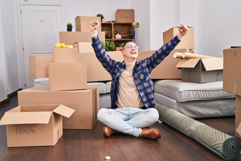Young Hispanic Man Sitting on Floor with Winner Expression at New Home ...