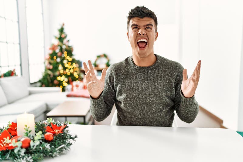 Young Hispanic Man Sitting on the Table by Christmas Tree Crazy and Mad ...