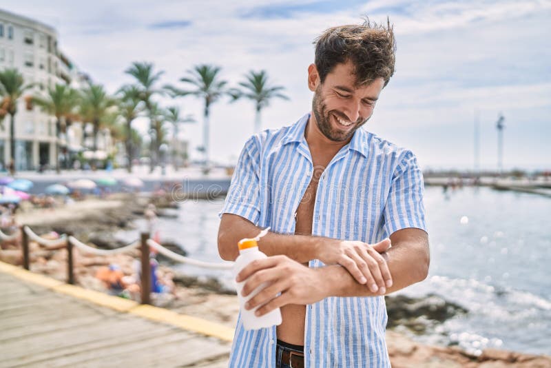 Young Hispanic Man Smiling Happy Using Sunscreen Lotion at the Beach ...