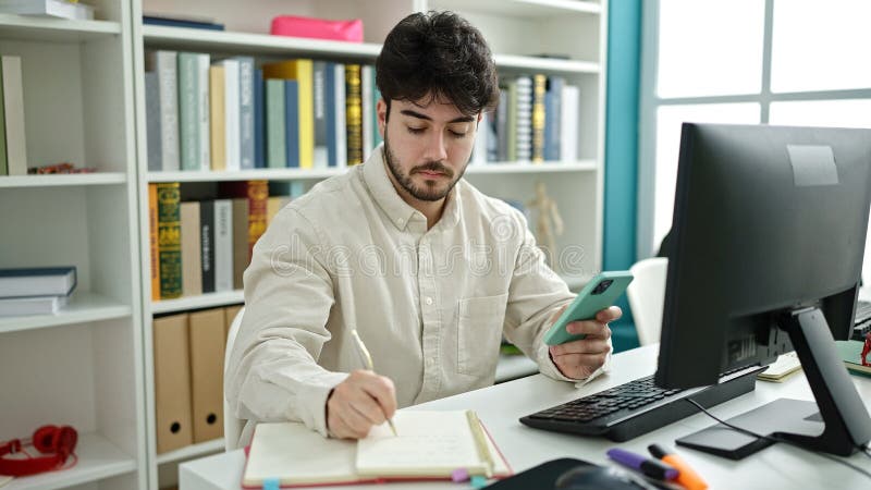 Young Hispanic Man Student Using Computer and Smartphone Writing Notes ...
